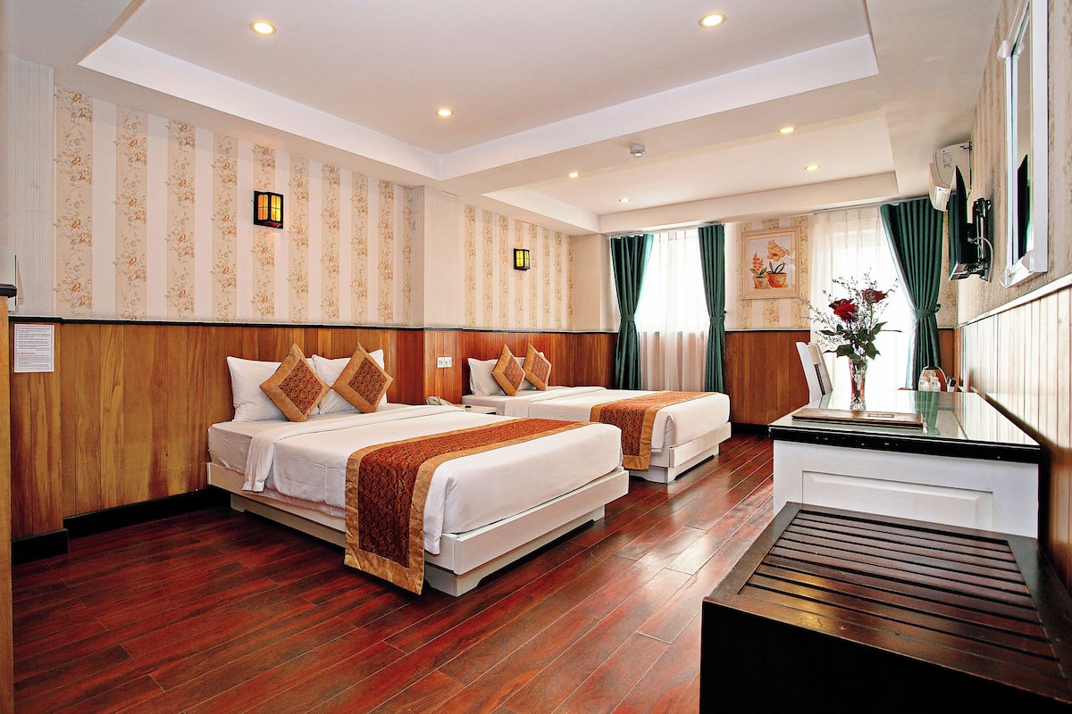 Quarto de hotel com duas camas, piso de madeira e uma pequena escrivaninha com espelho.