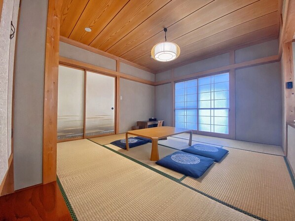 Um quarto japonês tradicional com tatames, uma mesa de madeira baixa, portas deslizantes e uma janela grande.