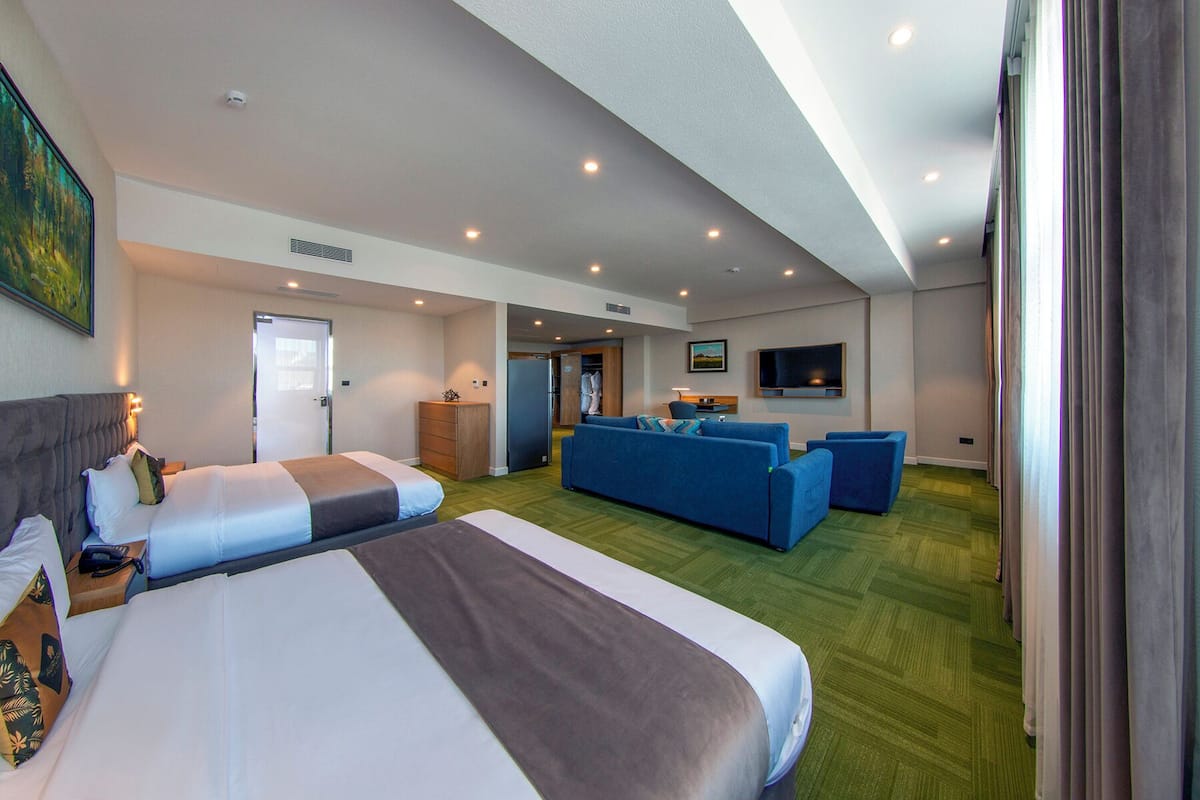 Quarto de hotel com uma cama grande, um sofá, uma televisão e um espaço de refeições.