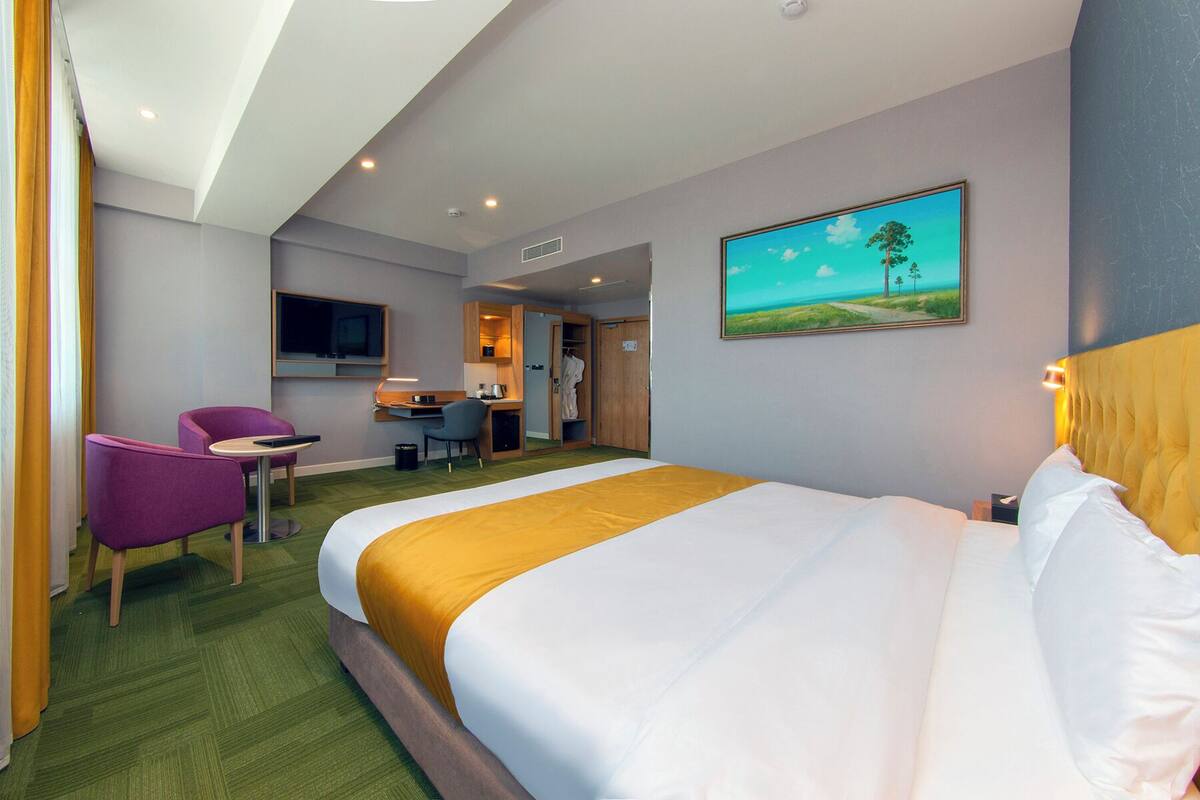 Quarto de hotel com uma cama grande, uma escrivaninha, uma cadeira e uma televisão.