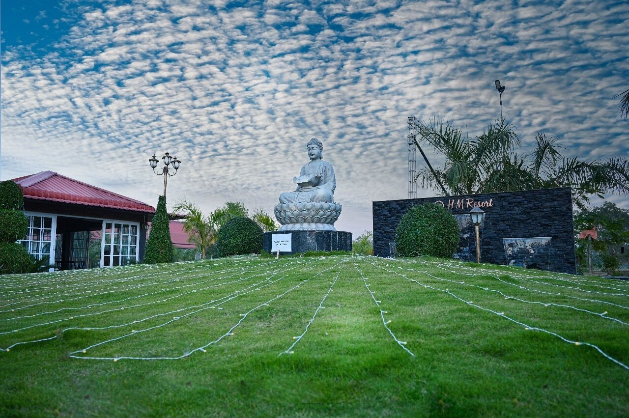 Uma estátua de Buda em uma área gramada sob um céu claro.