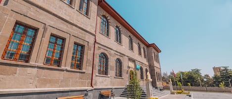 Um edifício com grandes janelas, fachada de pedra e um espaço pavimentado com bancos.