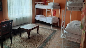 Um quarto de dormitório com beliches, uma cadeira de madeira, uma mesinha e um tapete estampado.