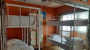 Quarto de estudante com beliches, soalho de madeira e janela com cortinas.