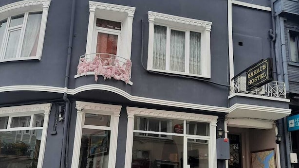 Um edifício de dois andares com fachada escura, detalhes brancos e uma placa indicando que é um albergue.
