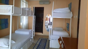 Um quarto de estudante com beliches, uma mesinha e um tapete.
