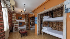 Um dormitório com beliches, um banco de madeira, cortinas estampadas e um ventilador de teto.