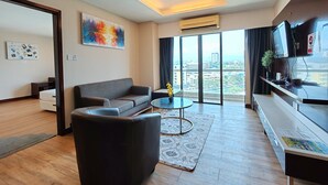 Uma sala de estar moderna com sofá, poltrona, mesa de centro e vista para a cidade através de grandes janelas.