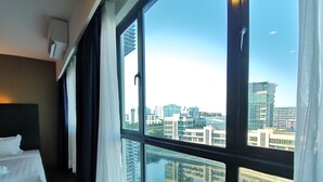 Quarto de hotel com uma janela grande, uma cama e vista para a cidade.