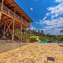 Área da piscina com piso em azulejos, deck de madeira e vista para um morro com casas.