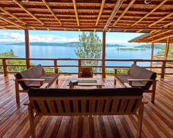 Um deck de madeira com dois sofás e uma mesa, com vista para um lago e uma ilha ao longe.