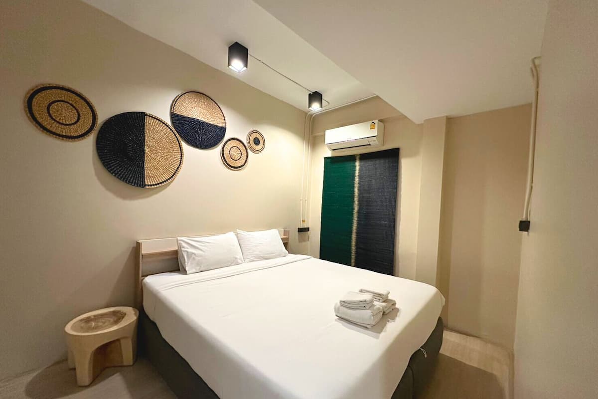 Um quarto moderno com uma cama grande, um banquinho de madeira pequeno e arte de parede trançada decorativa.