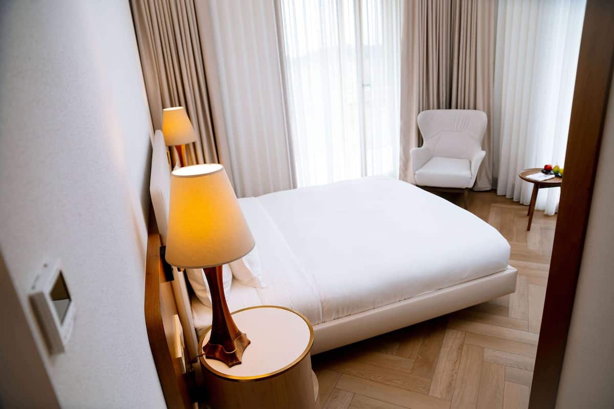 Quarto de hotel com cama, uma cadeira, uma mesinha com frutas e um abajur.