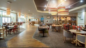 Um restaurante espaçoso com piso de madeira, várias áreas de refeições e luminárias pendentes listradas e coloridas.