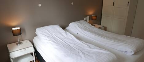 Uma cama de casal com roupa de cama branca, uma mesa de cabeceira com abajur e um guarda-roupa em um quarto de hotel.