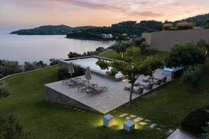 Área externa ajardinada com piscina, área de estar e vista para o mar.