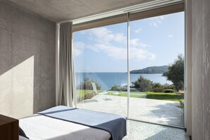 Quarto com uma grande porta de vidro deslizante que dá para uma varanda com vista para o mar e uma ilha distante.