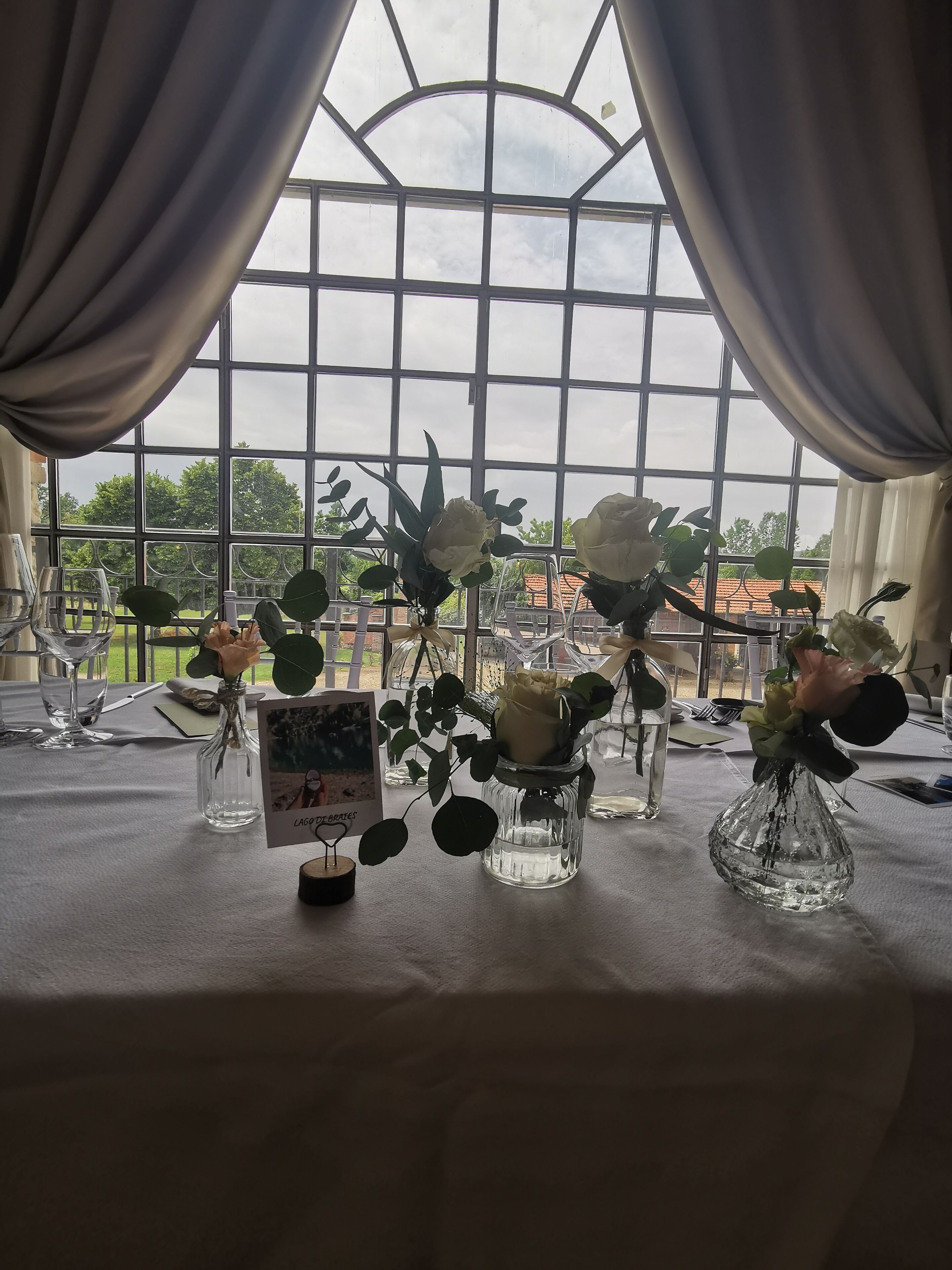Mesa posta para refeição, com vasos de flores e uma placa com a inscrição 