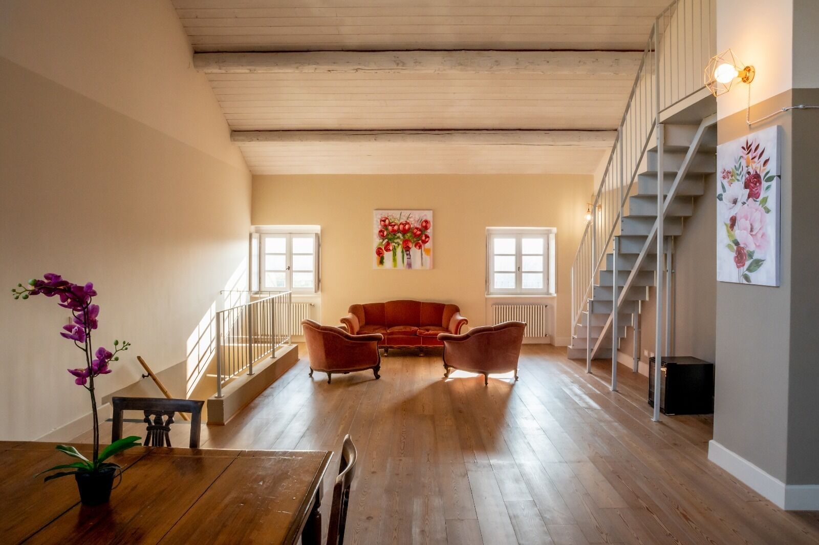 Um amplo loft com teto alto, escada de madeira, sofá vermelho e área de jantar com mesa e cadeiras.