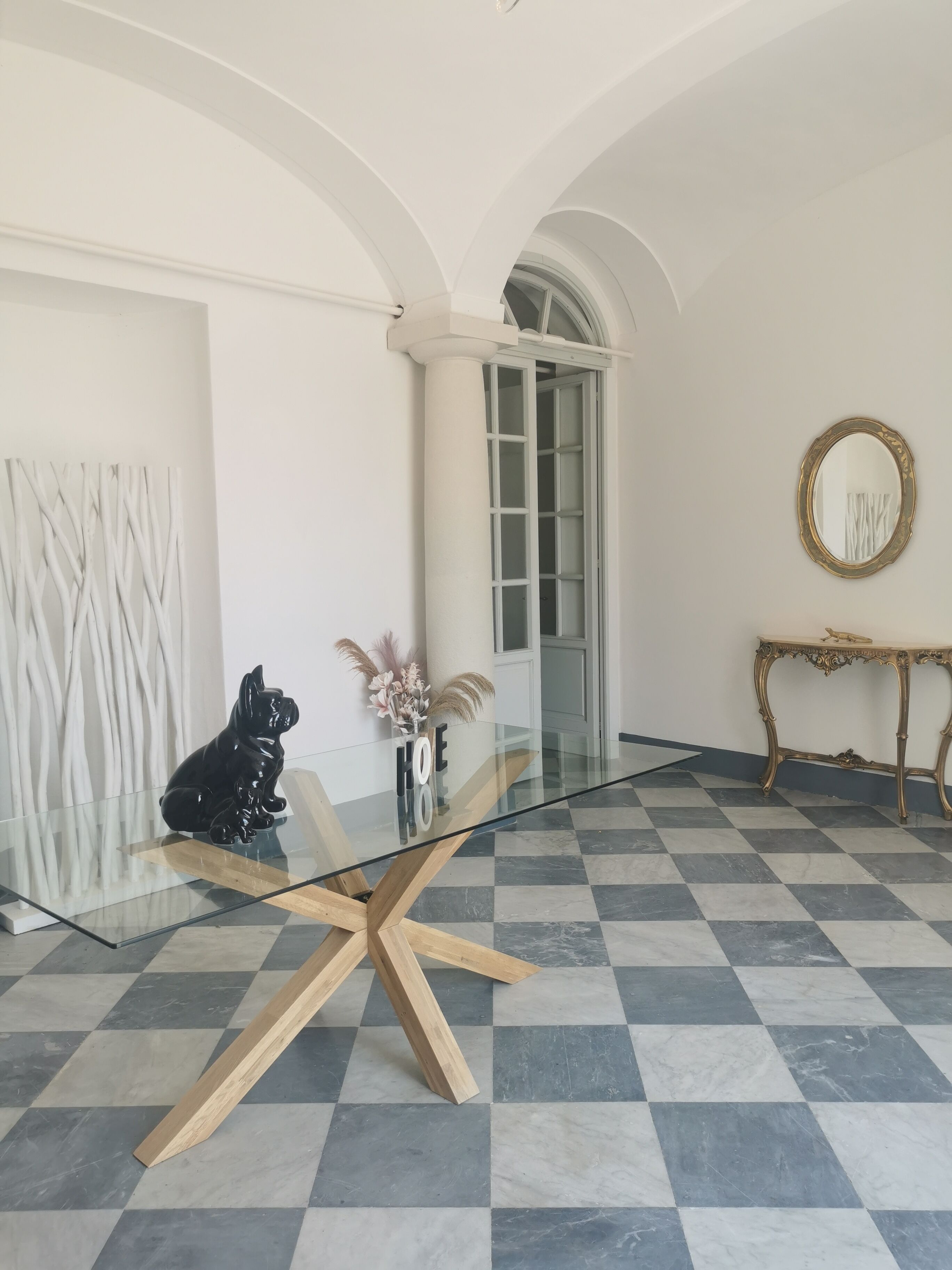 Um quarto espaçoso com uma mesa de vidro, uma estátua decorativa de cachorro e um chão xadrez.