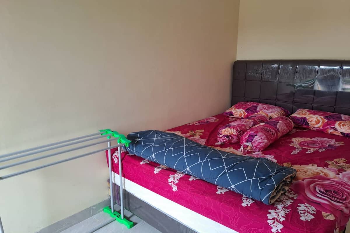 Cama com colcha florida e travesseiro azul escuro, varal de metal e tapete de chão verde.