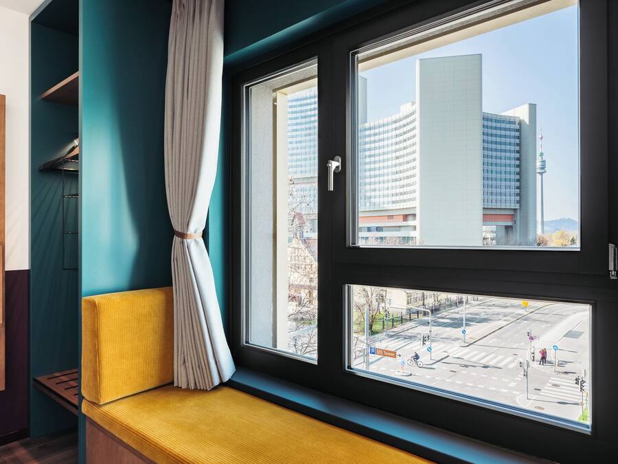 Quarto com vista para a paisagem urbana através de uma janela, um banco e uma porta com cortina.