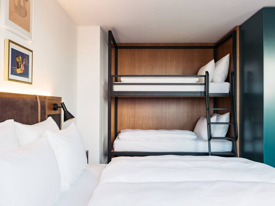 Uma cama beliche com roupa de cama branca, cabeceira de madeira e escada preta.