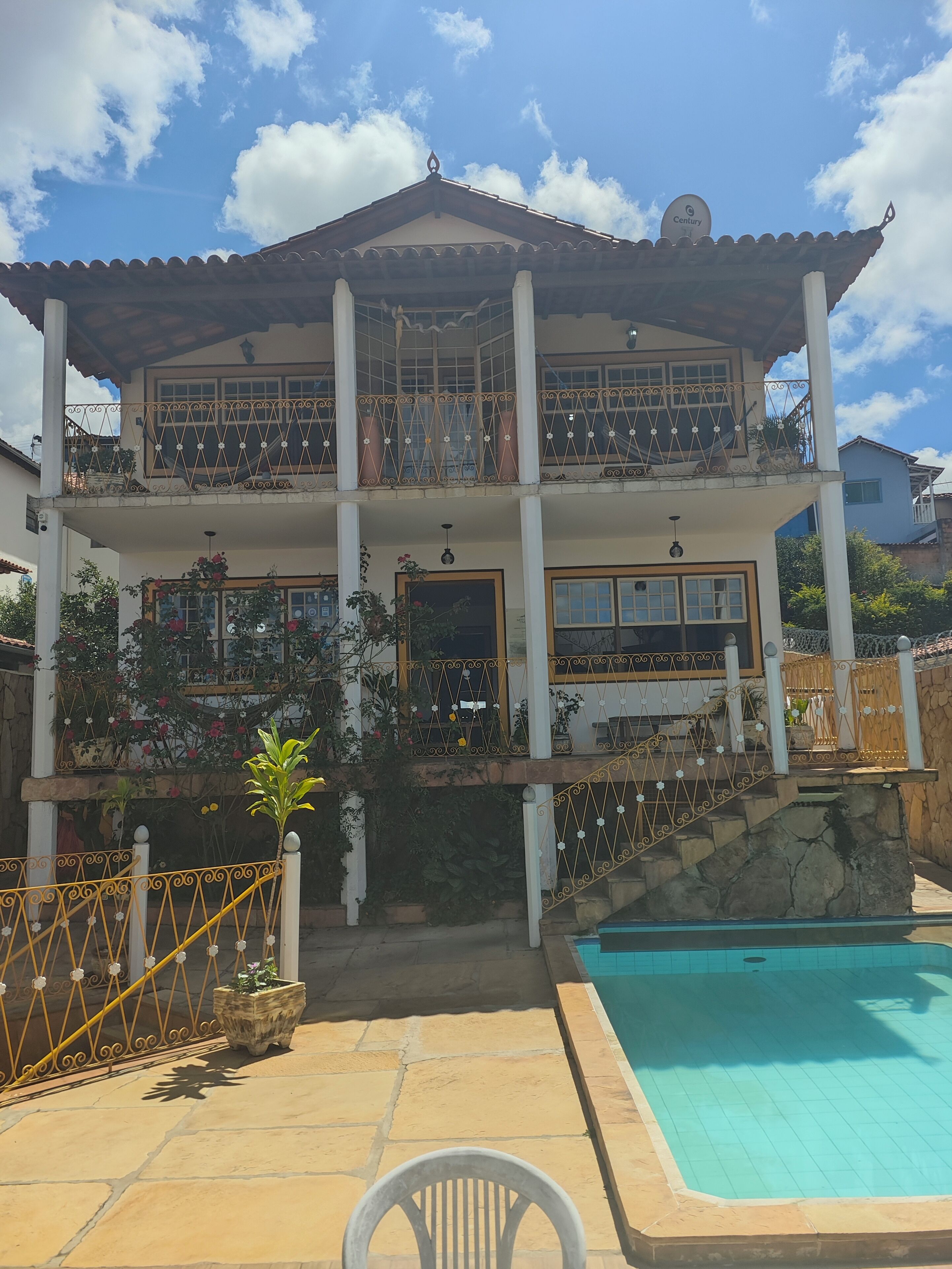Uma casa de dois andares com varanda, piscina e antena parabólica.