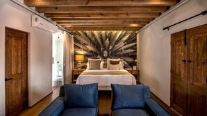 Quarto com cama grande, vigas de madeira no teto e dois sofás azuis.