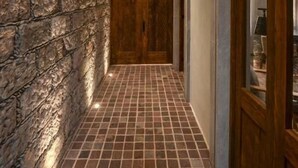 Um corredor com parede de pedra, porta de madeira e chão de azulejos.