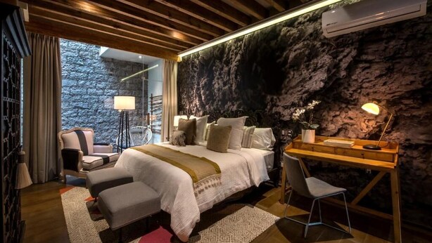 Quarto com cama, escrivaninha, cadeira, luminária e vista para o exterior.