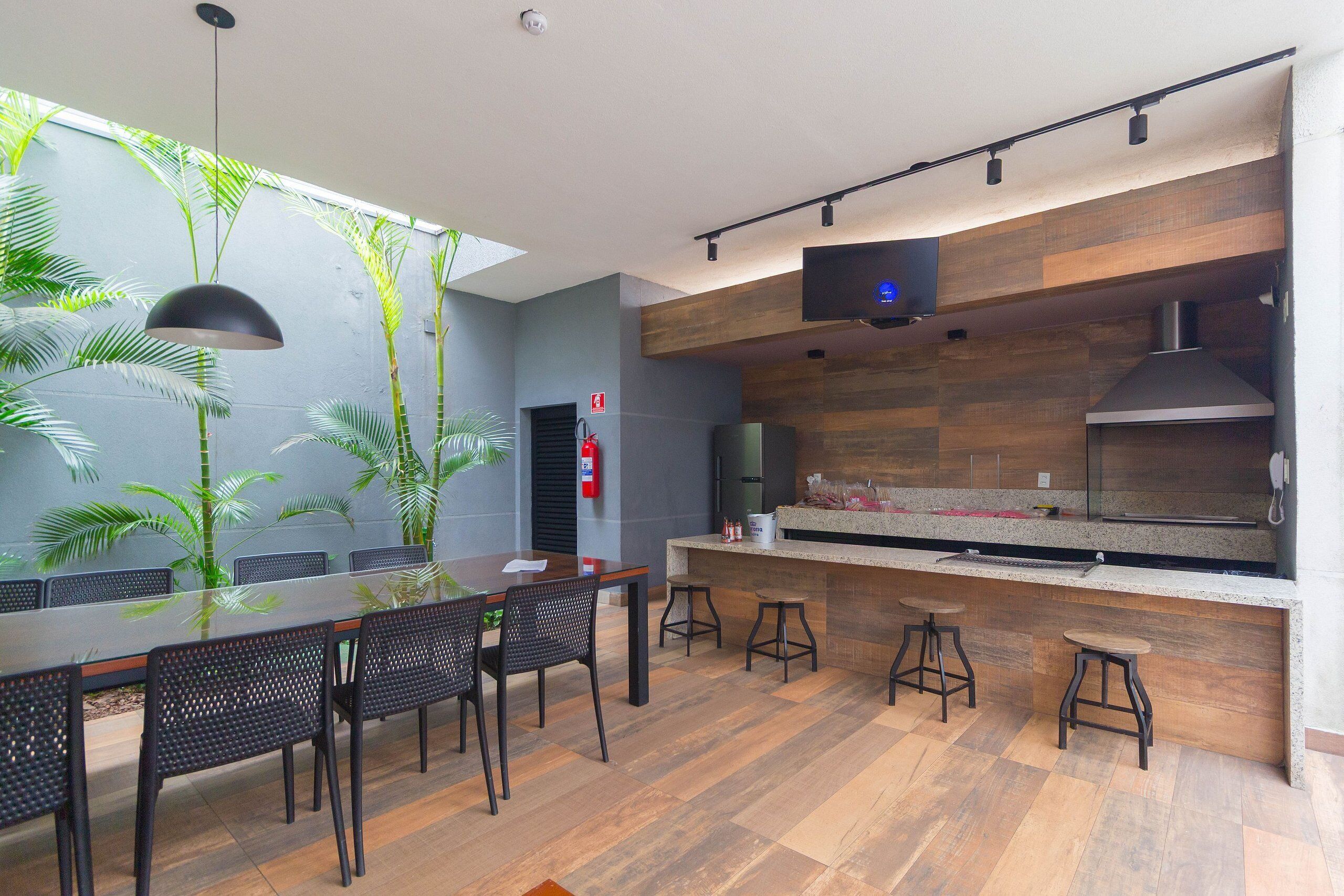 Uma cozinha moderna com painel de madeira, ilha integrada com banquetas e área de refeições com mesa e cadeiras de vidro.