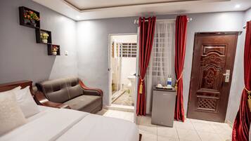 Quarto de hotel com uma cama, um sofá, uma mesinha com uma garrafa e uma porta com painel decorativo.