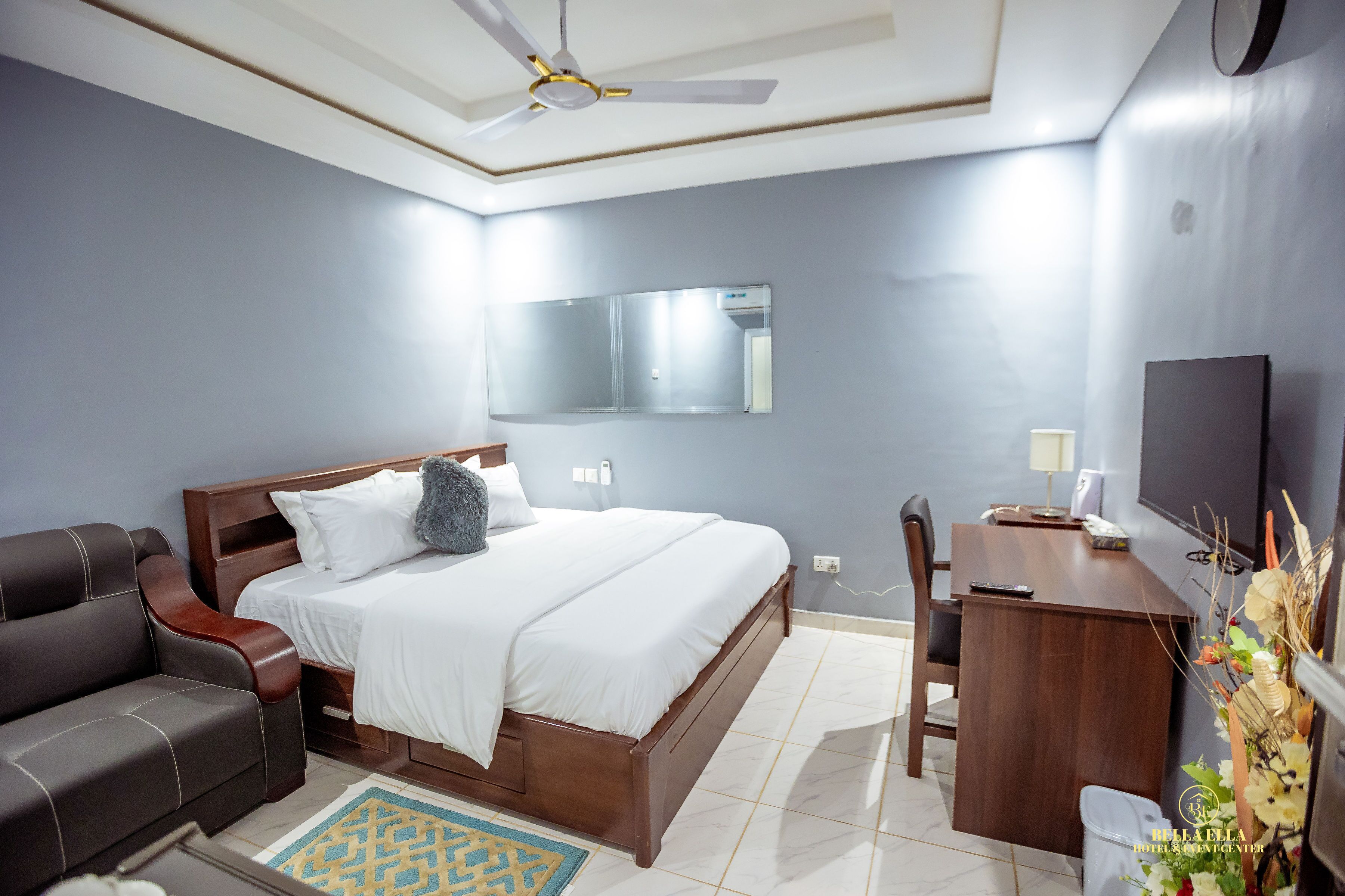 Quarto de hotel moderno com cama, escrivaninha, sofá e televisão.