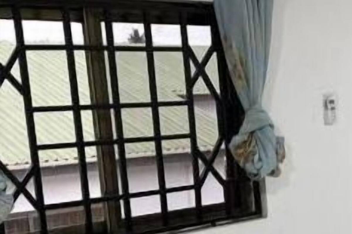 Quarto com janela de grades de metal preto, parede branca e chão de azulejos.