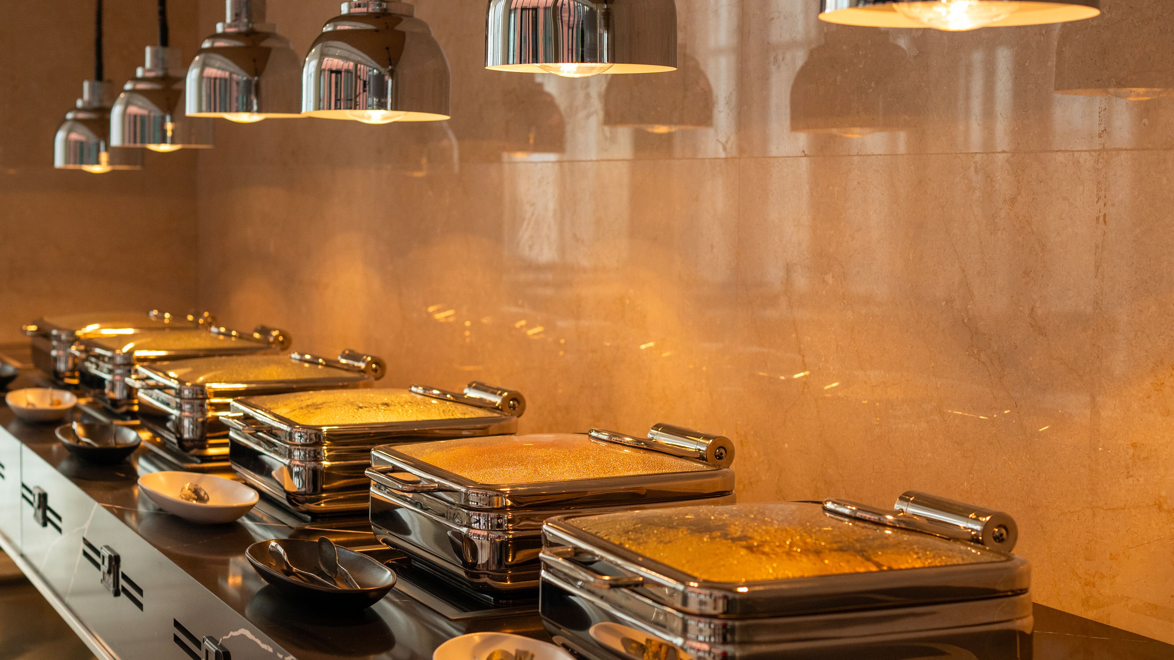 Disposição de buffet com várias estações de serviço, cada uma com um recipiente para alimentos coberto e uma tigela.