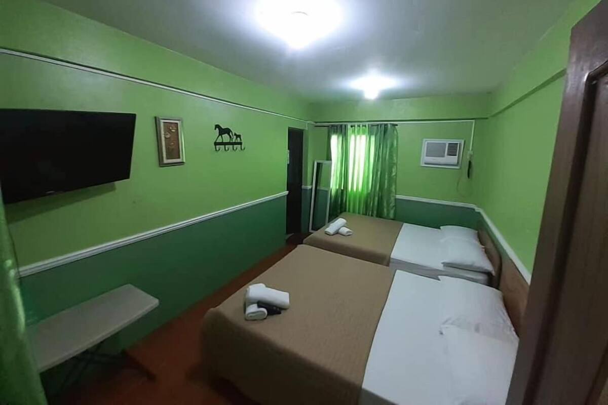 Quarto de hotel com duas camas, televisão de tela plana, uma mesinha e ar condicionado fixado na parede.