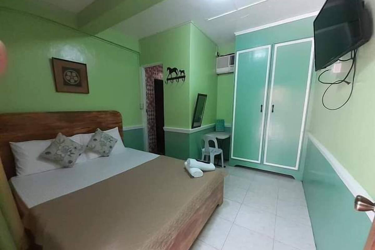 Quarto com cama, escrivaninha, guarda-roupa e televisão.