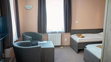 Quarto de hotel com cama, escrivaninha, cadeira e televisão.