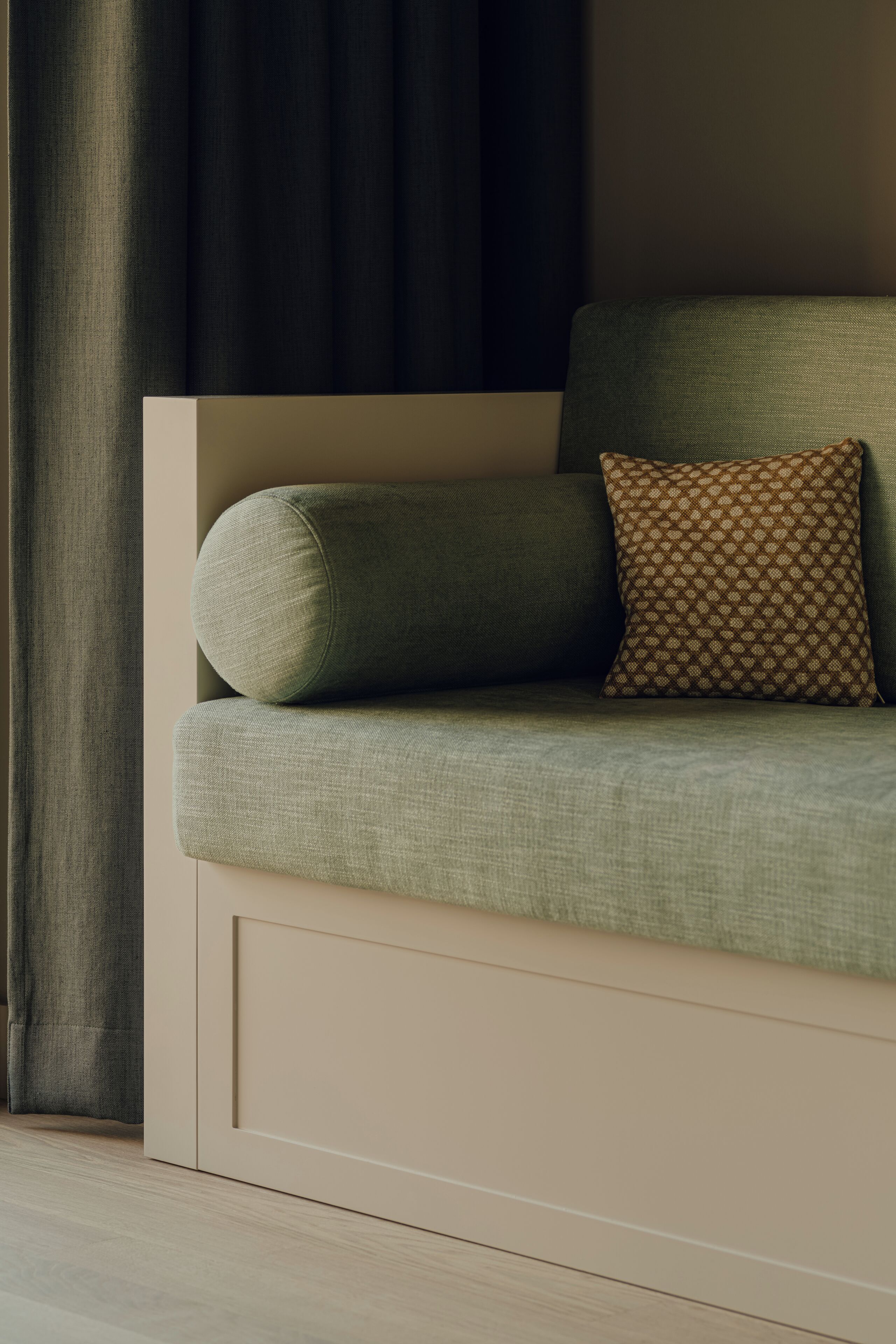 Um sofá moderno com almofada estampada em um quarto minimalista, com piso de madeira e cortinas escuras.