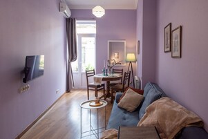 Uma sala de estar com televisão, sofá, mesa de jantar, cadeiras e uma luminária.
