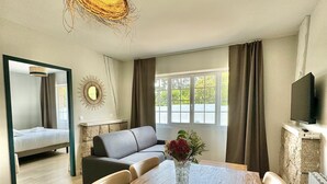 Uma sala de estar moderna com uma mesa de jantar de madeira, um sofá, uma TV e uma janela grande com cortinas.