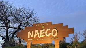 Uma placa de madeira com o texto 'ERDEVEN NAECO' e as palavras 'DORMIR • RELAXAR • CONVIVIALIDADE', indicando um local para descanso e relaxamento.
