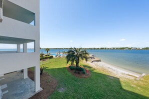 Vista de uma praia com piscina, palmeiras e um edifício branco.