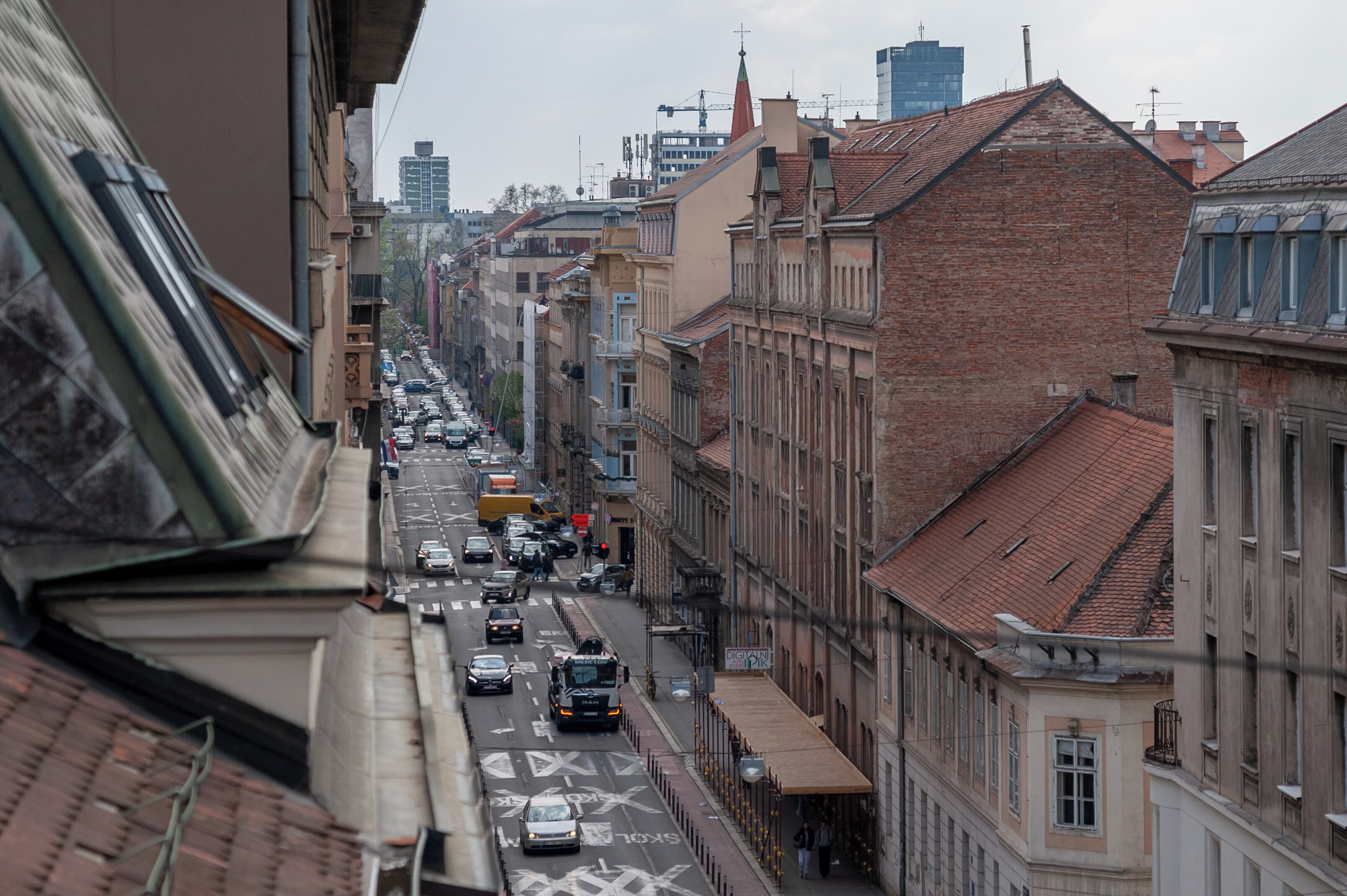 Vista da rua com edifícios, carros e céu claro.