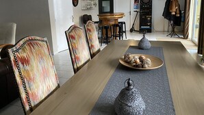 Uma sala de jantar com uma mesa de madeira comprida, cadeiras estampadas, um tabuleiro decorativo com pão e um candeeiro.