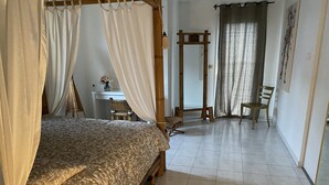 Quarto com cama de dossel, mesa de cabeceira, cadeira, espelho e janela com cortinas.