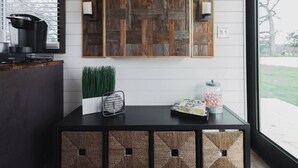 Cozinha moderna com bancada preta, cafeteira, planta em vaso e painel decorativo na parede.