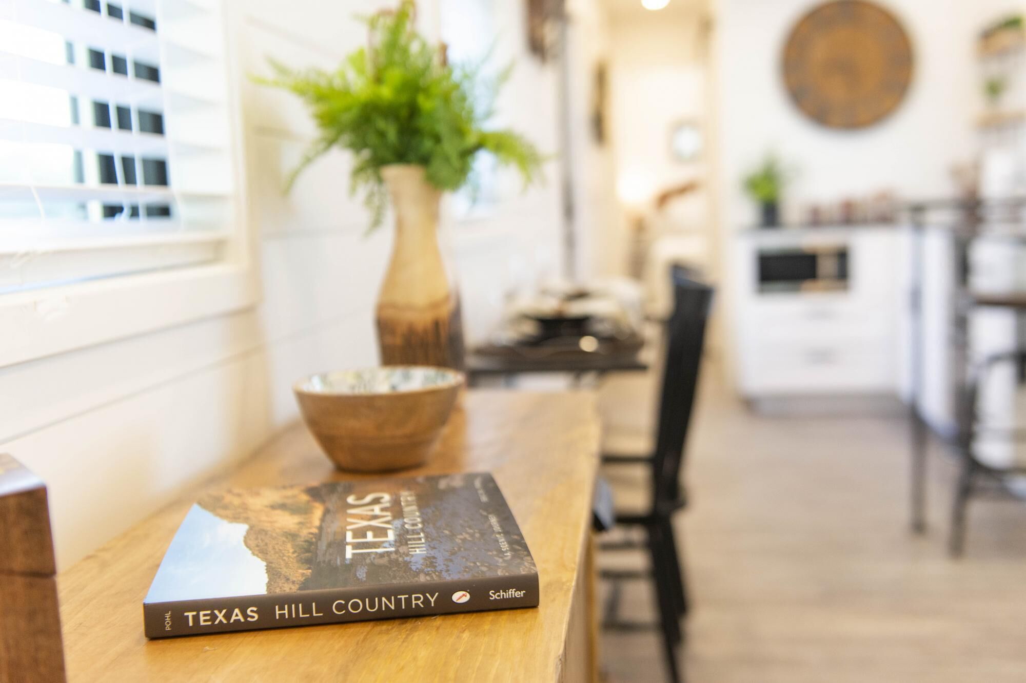 Um livro intitulado 'Texas Hill Country' sobre uma mesa de madeira em um quarto bem iluminado, com uma planta e uma tigela.