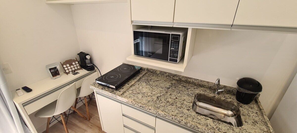 Uma cozinha compacta com micro-ondas, torradeira e cafeteira sobre uma bancada de granito.